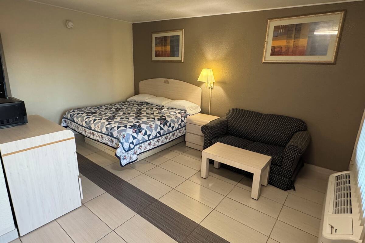 Quarto de hotel com uma cama, um sofá, uma escrivaninha e uma luminária.