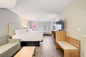 Quarto de hotel com cama, sofá, escrivaninha, banco, televisão e janela com vista.
