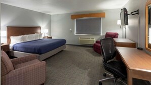 Quarto de hotel com cama, escrivaninha, cadeira, televisão e janela.