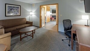 Quarto de hotel com sofá, uma pequena mesa, escrivaninha com cadeira, televisão e lareira ao fundo.