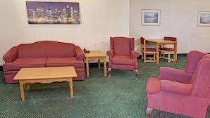 Um quarto com um sofá vermelho, uma mesa de centro de madeira, uma pequena mesa lateral, uma poltrona vermelha e uma mesa de jantar de madeira com duas cadeiras vermelhas.