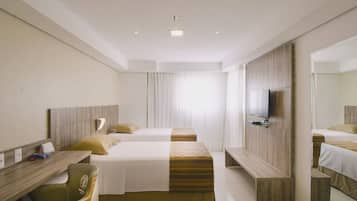 Quarto de hotel com duas camas, uma escrivaninha, uma cadeira, uma televisão e um espelho grande.
