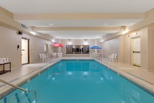 Piscina interna com faixas demarcadas, dois guarda-sóis e cadeiras brancas ao redor da área da piscina.