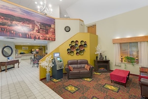 Um saguão de hotel com escadas, um balcão de recepção, uma área de estar com sofá e poltronas, uma parede decorativa com espelhos circulares e uma lareira.