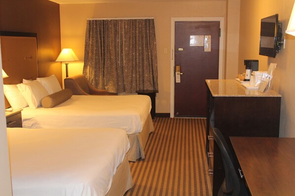 Quarto de hotel com duas camas, uma escrivaninha, uma televisão e uma porta.
