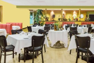 Um restaurante com mesas redondas, cadeiras pretas e uma parede amarela.