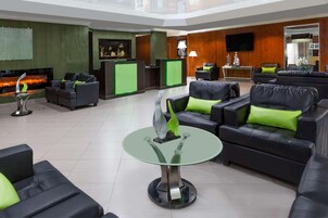 Um hall de hotel com sofás de couro, uma mesa de vidro, balcão de recepção e lareira.
