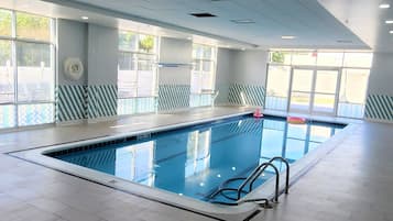 Piscina interna com água azul cristalina, escada de acesso e vista para o exterior através de amplas janelas.