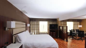 Quarto de hotel com cama, escrivaninha, televisão e área de estar com cadeiras.