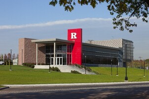 Um edifício moderno com um grande letreiro vermelho em formato de 'R', entrada de vidro e gramado bem cuidado.