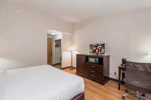 Quarto de hotel com cama, escrivaninha com computador, televisão, micro-ondas e máquina de café.