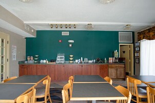 Uma área de refeições com mesas e cadeiras de madeira, um balcão de bar com diversos objetos e uma parede verde.