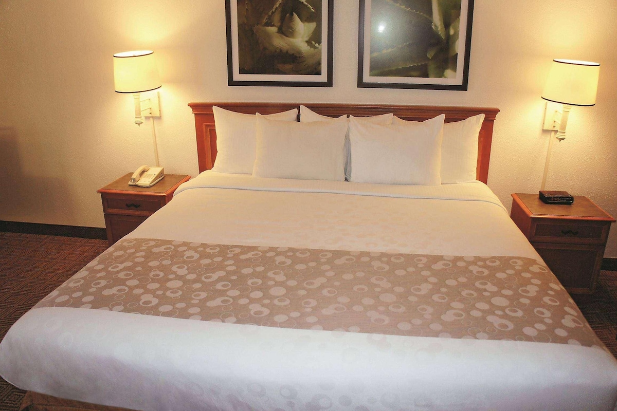 Quarto de hotel com cama, duas mesas de cabeceira, telefone e duas luminárias fixadas na parede.