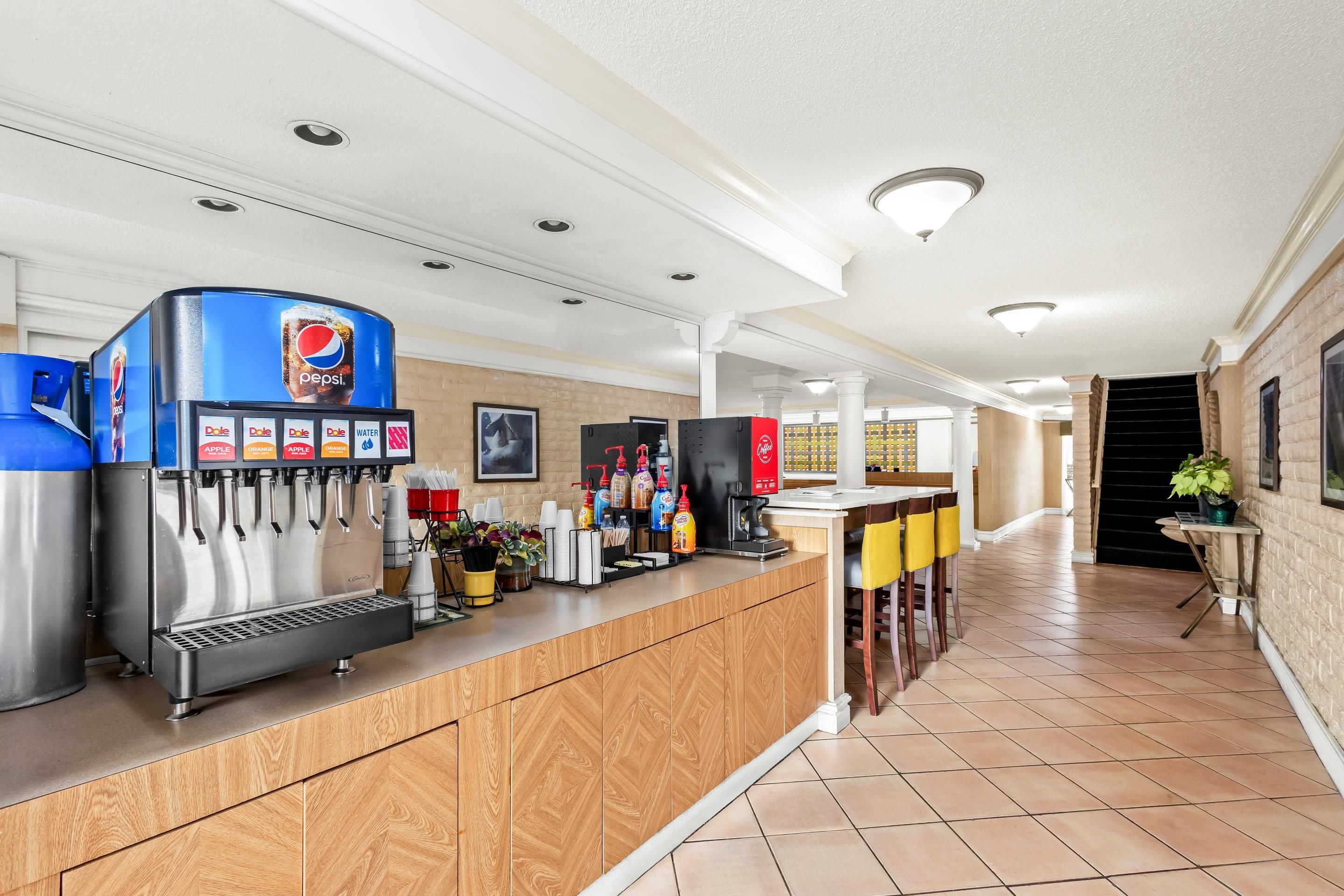 Uma área de bar moderna e bem cuidada, com máquina de refrigerantes Pepsi, máquina de café e diversos condimentos.