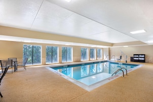 Piscina interior com janelas amplas, área de estar à beira da piscina e piso revestido de azulejos.