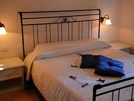Cama com estrutura de metal, roupa de cama branca e duas luminárias de cabeceira.
