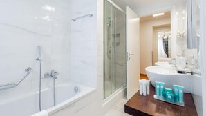 Casa de banho moderna com chuveiro em cabine de vidro, banheira e lavatório com um grande lavabo e produtos de higiene pessoal.