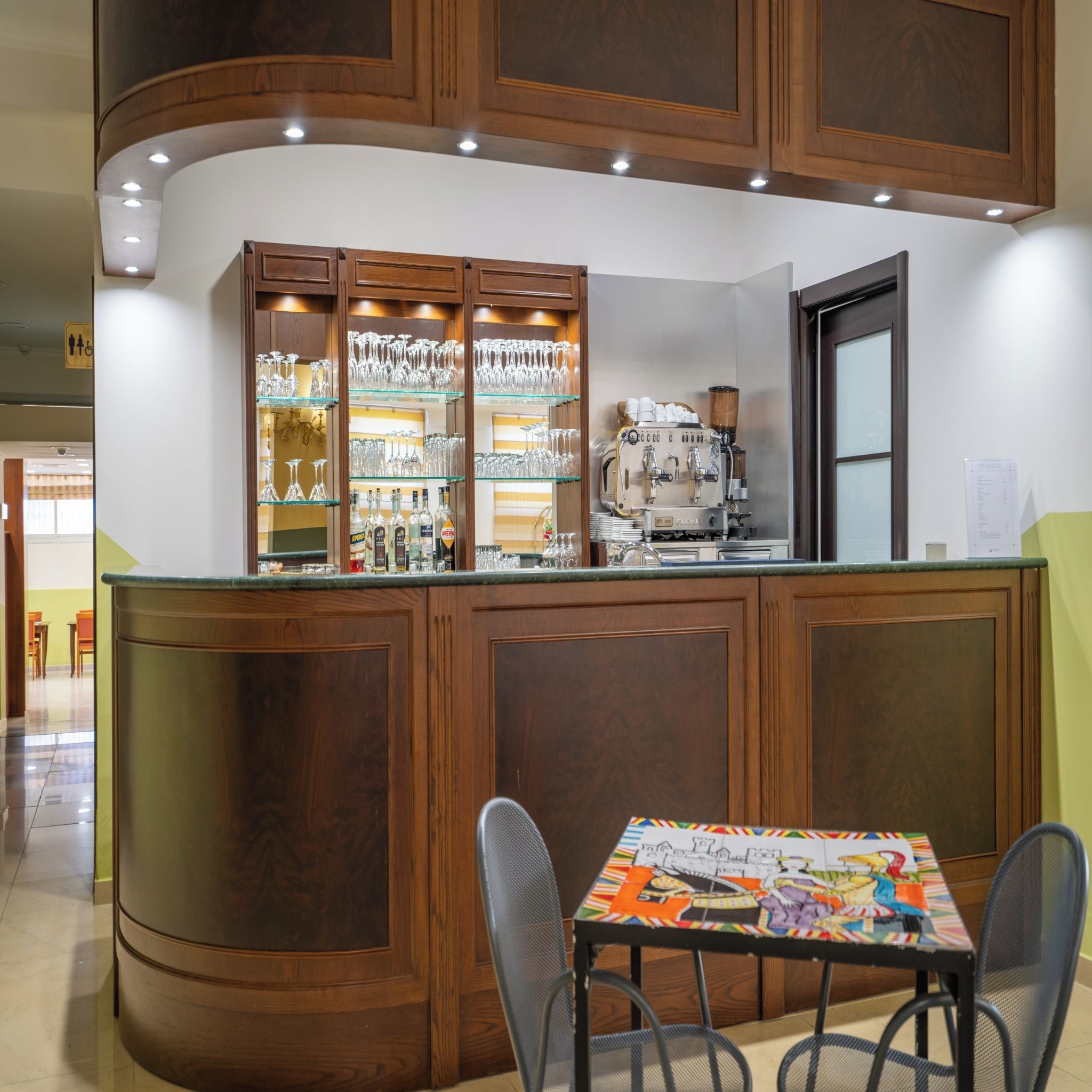 Uma área de bar com armários de madeira, uma máquina de café e uma mesa com cadeiras.