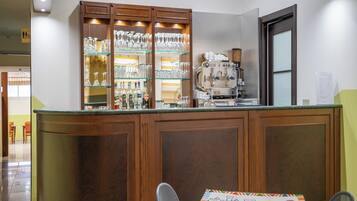 Uma área de bar com armários de madeira, uma máquina de café e uma mesa com cadeiras.