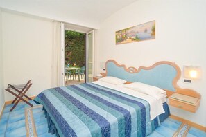 Quarto com cama, mesa de cabeceira, quadro e vista de um jardim através de uma porta aberta.