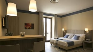 Quarto de hotel com uma cama, duas mesas de cabeceira, uma escrivaninha com cadeira, uma televisão e uma janela grande com cortinas.