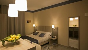 Quarto de hotel moderno com cama, mesas de cabeceira, escrivaninha e espelho.