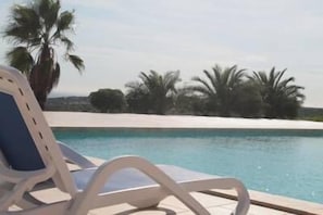 Uma área junto à piscina com espreguiçadeiras e palmeiras.
