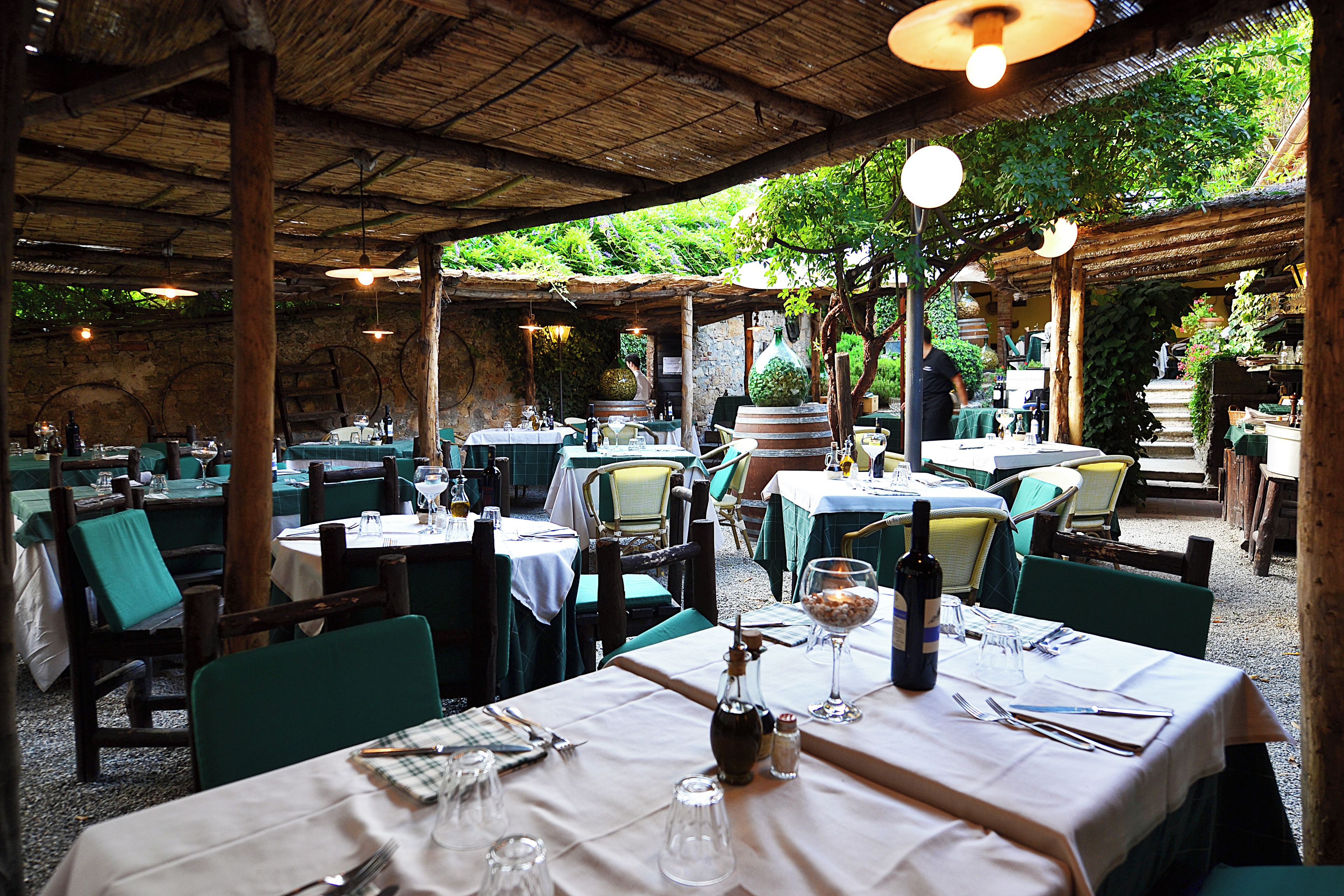 Um restaurante ao ar livre com mesas e cadeiras, coberto por um telhado de madeira e rodeado por vegetação.
