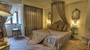 Quarto com cama grande, uma cadeira, mesa de cabeceira com abajur e janela com cortinas.