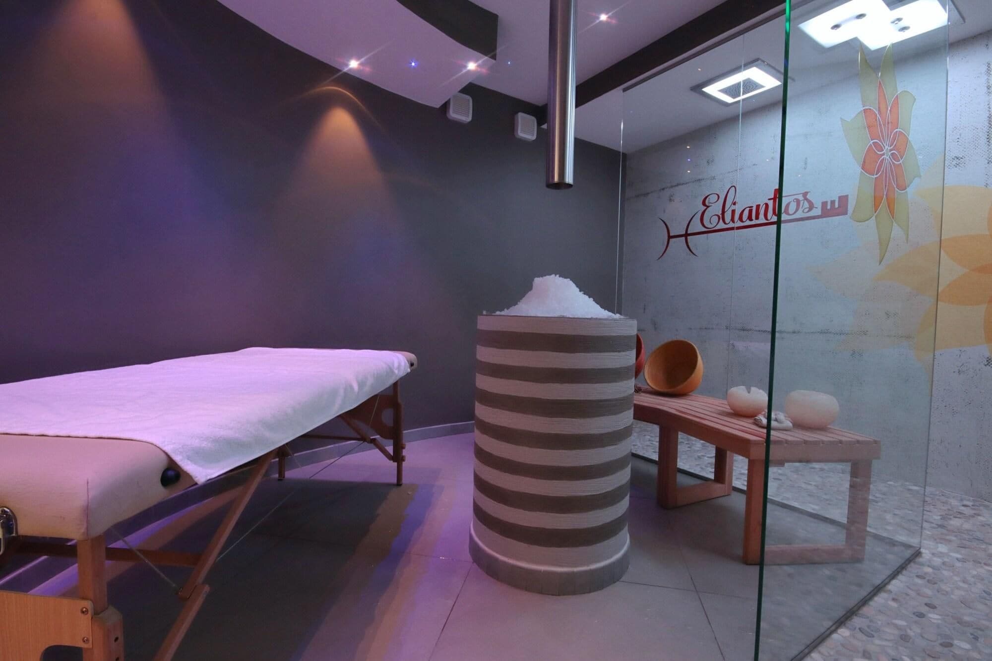 Um spa moderno com uma mesa de massagem, um pilar listrado e uma pequena mesa de madeira com objetos decorativos.