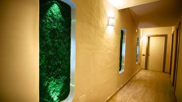 Um corredor com um painel de parede iluminado em verde, piso de madeira e uma porta com desenho floral.