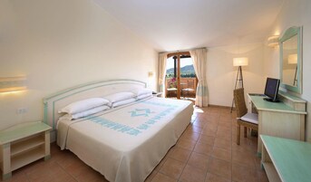 Quarto de hotel com cama, escrivaninha com computador, cadeira e varanda com vista.
