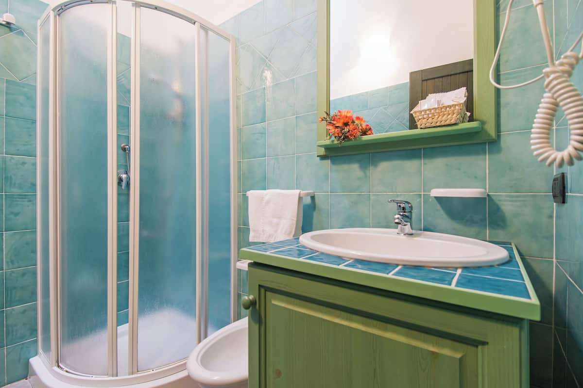 Uma casa de banho com cabine de duche em vidro, uma pia com bancada verde e um espelho sobre a pia.