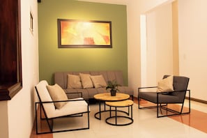Uma sala de estar com sofá, duas poltronas, mesa de centro e um quadro na parede.