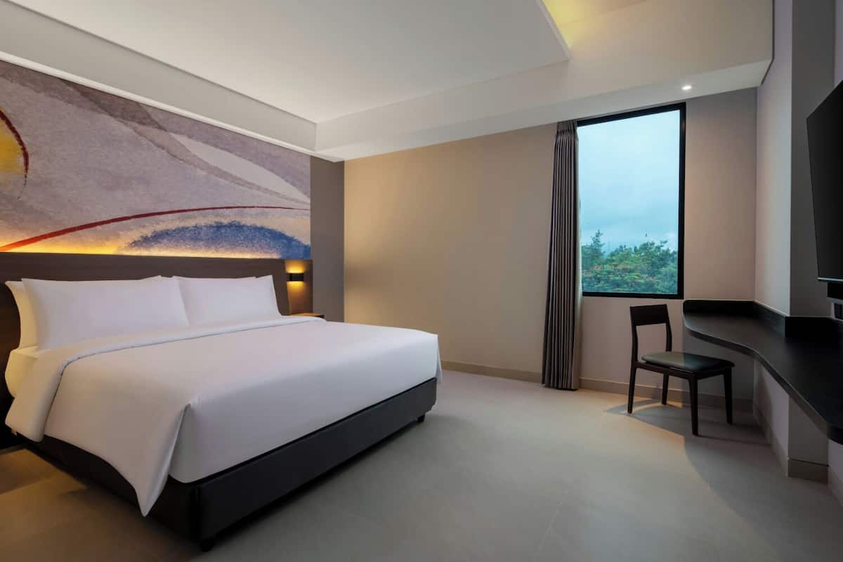 Quarto de hotel moderno com uma cama grande, uma escrivaninha e uma janela com vista para o verde.