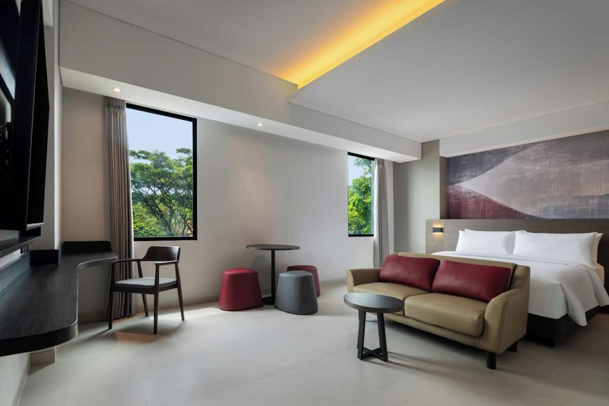 Quarto de hotel moderno com uma cama grande, um sofá, uma mesa de jantar e uma televisão.