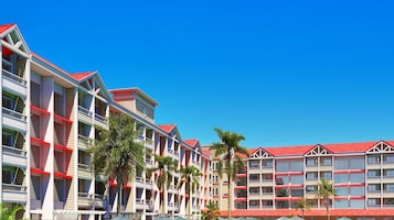 Um hotel com vários andares, varandas, telhados vermelhos e palmeiras.
