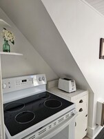 Cozinha com fogão branco, torradeira e prateleira pequena com garrafa verde e flores.