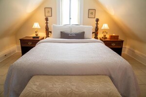 Cama bem arrumada com colcha e almofadas estampadas, flanqueada por duas mesas de cabeceira com abajures e quadros na parede.
