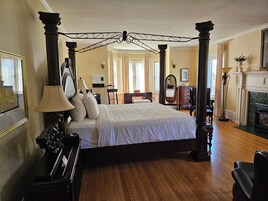 Um quarto espaçoso com uma cama de dossel, piso de madeira e lareira.