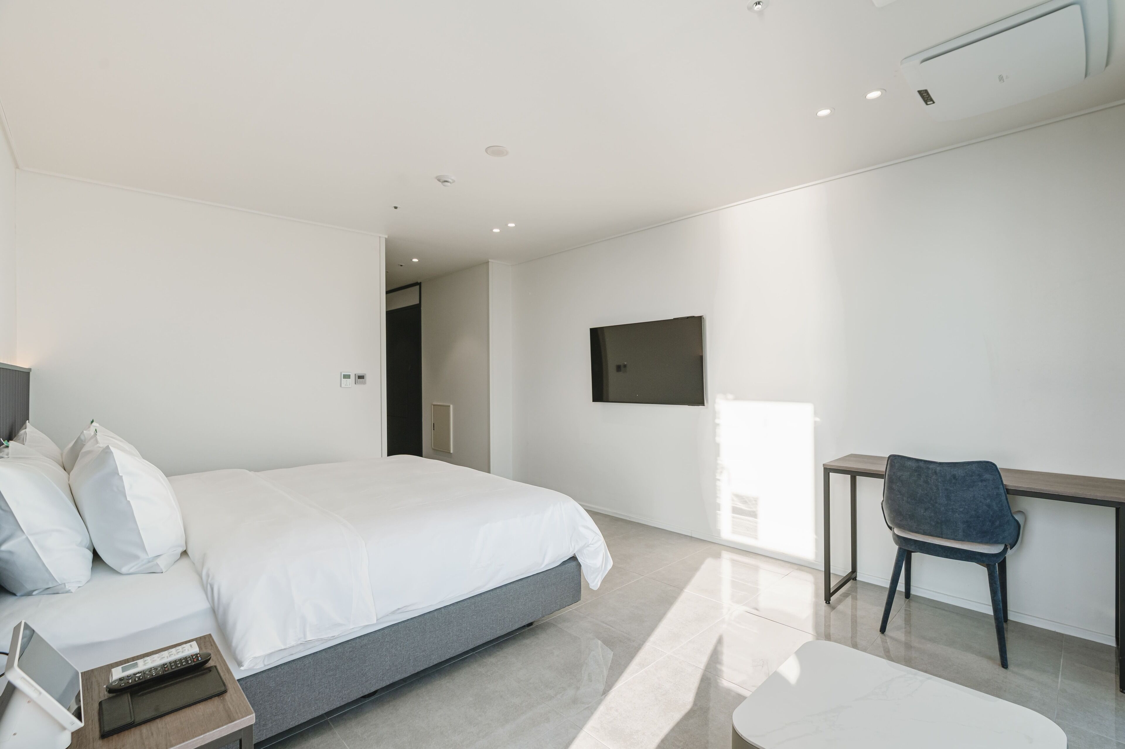 Quarto de hotel moderno com uma cama grande, uma escrivaninha, uma cadeira e uma televisão de tela plana na parede.