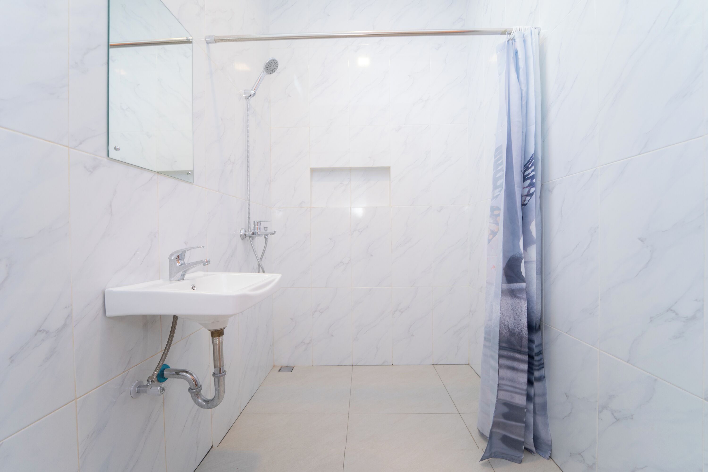 Casa de banho com lavatório branco, chuveiro e espelho.
