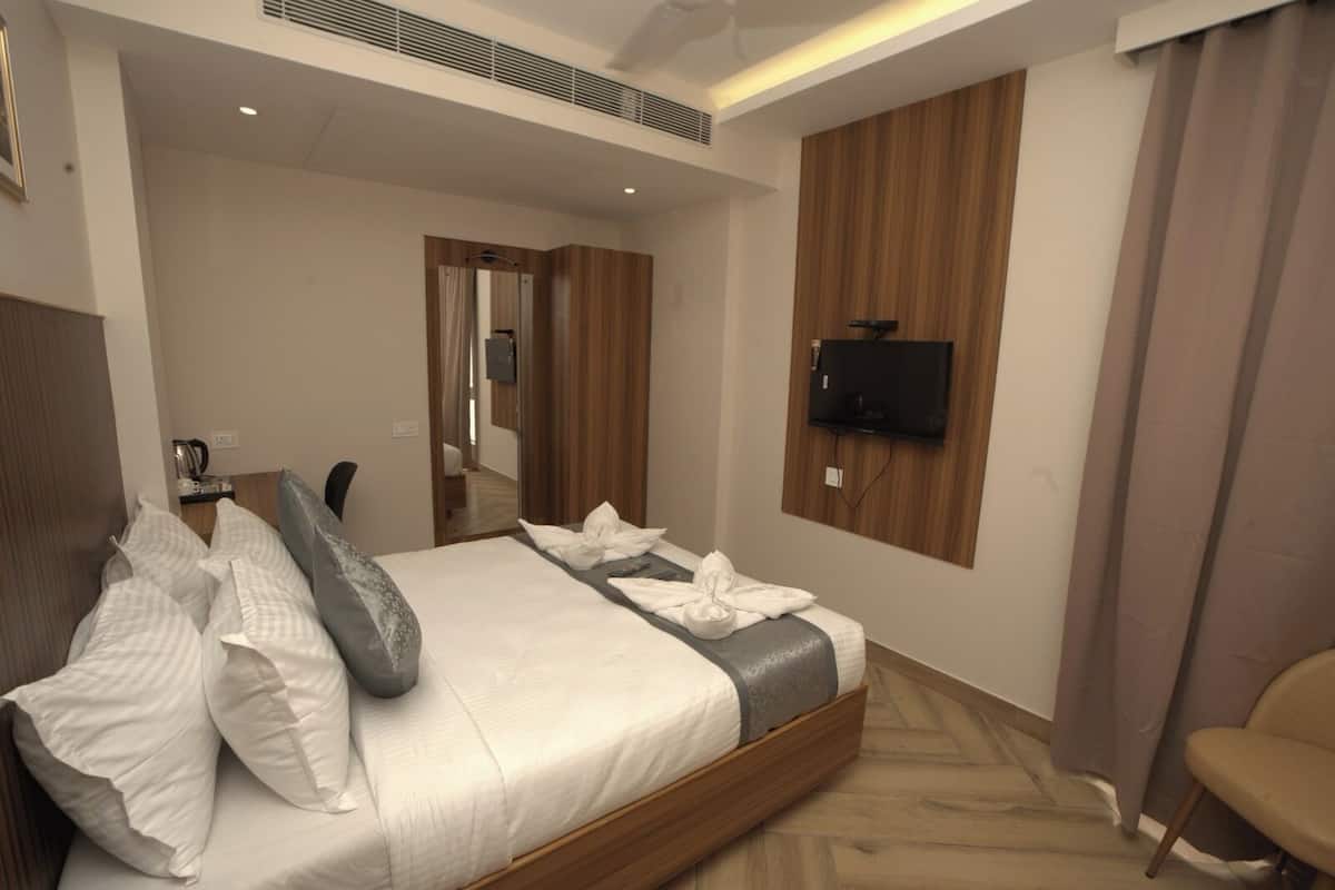Quarto de hotel com cama, televisão fixada na parede e piso de madeira.