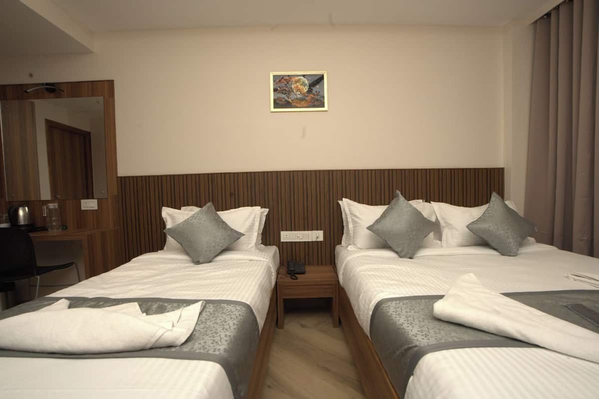 Quarto de hotel com duas camas, cabeceira de madeira, escrivaninha com cadeira, espelho e um quadro na parede.
