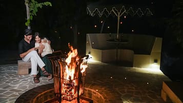 Um casal sentado perto de uma fogueira, com chão de pedra e área de estar moderna ao ar livre.