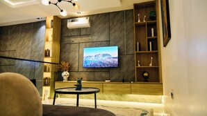 Uma sala de estar moderna com uma TV de tela plana fixada numa parede escura, uma mesa de centro redonda e um sofá.
