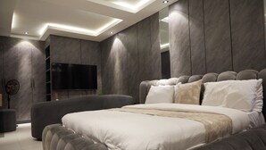Quarto moderno com uma cama grande, televisão de tela plana e guarda-roupa em tons escuros.