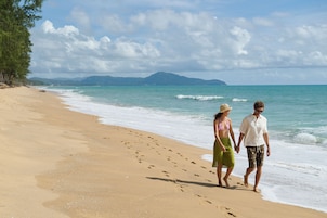 Uma praia com pegadas a levar à água, céu limpo e montanhas ao longe.
