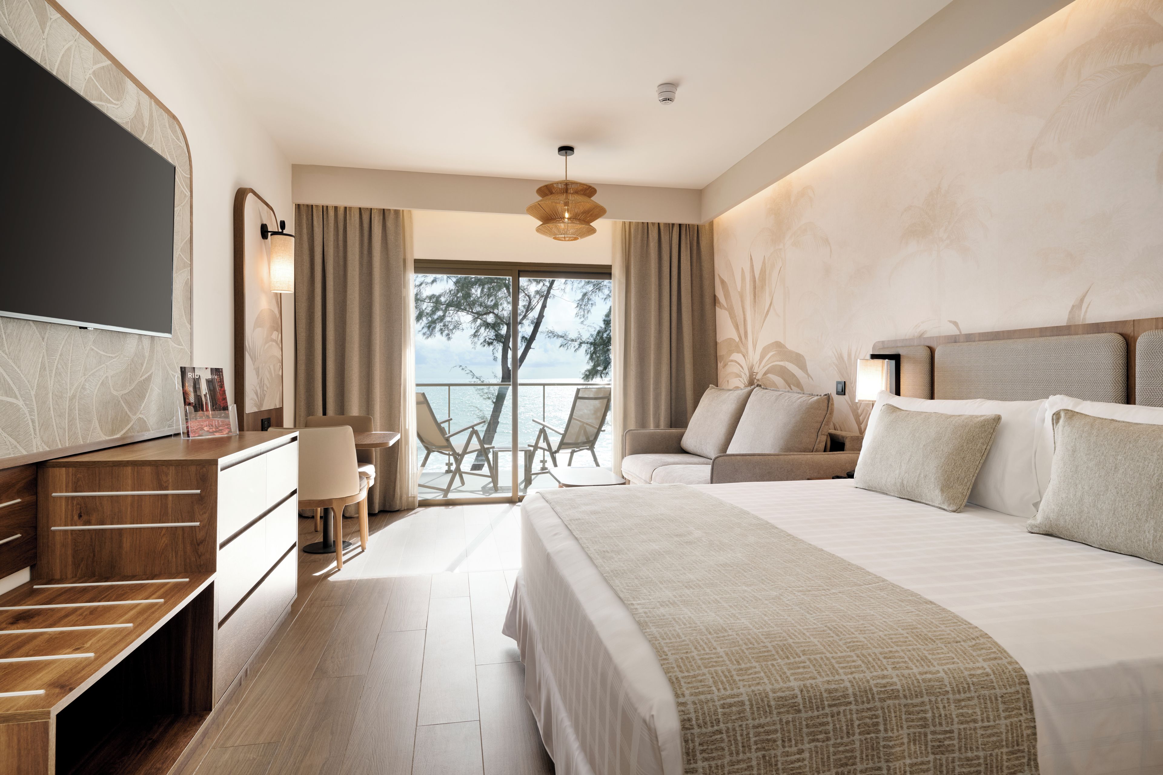 Quarto de hotel moderno com uma cama grande, uma escrivaninha, uma cadeira e uma varanda com vista para o mar.