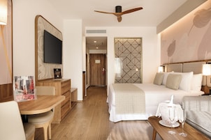 Quarto de hotel com cama, escrivaninha, televisão e ventoinha no teto.